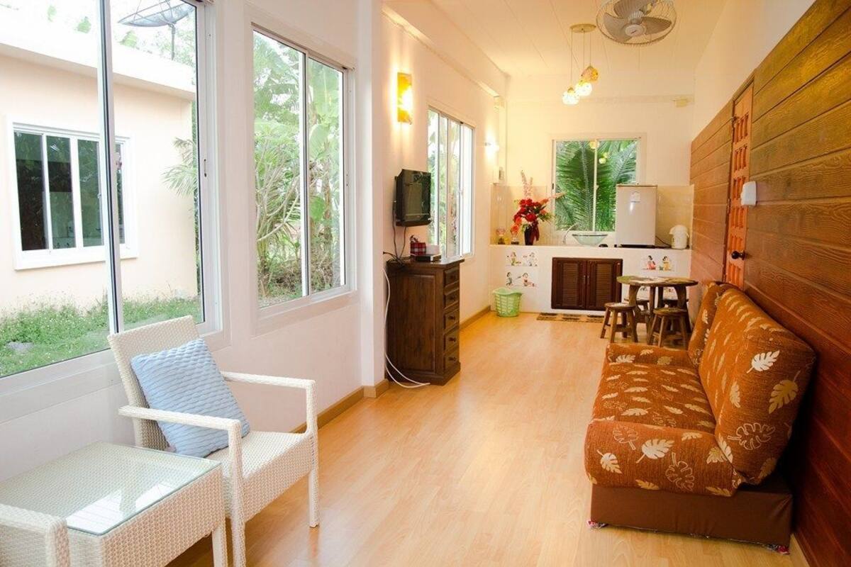 Uma sala de estar acolhedora com sofá, poltrona, televisão e uma área de cozinha com frigorífico e pia.