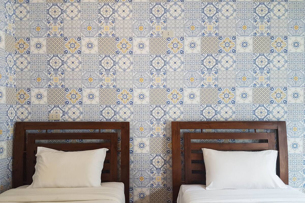 Quarto com duas camas apoiadas em parede com design de azulejos estampados.