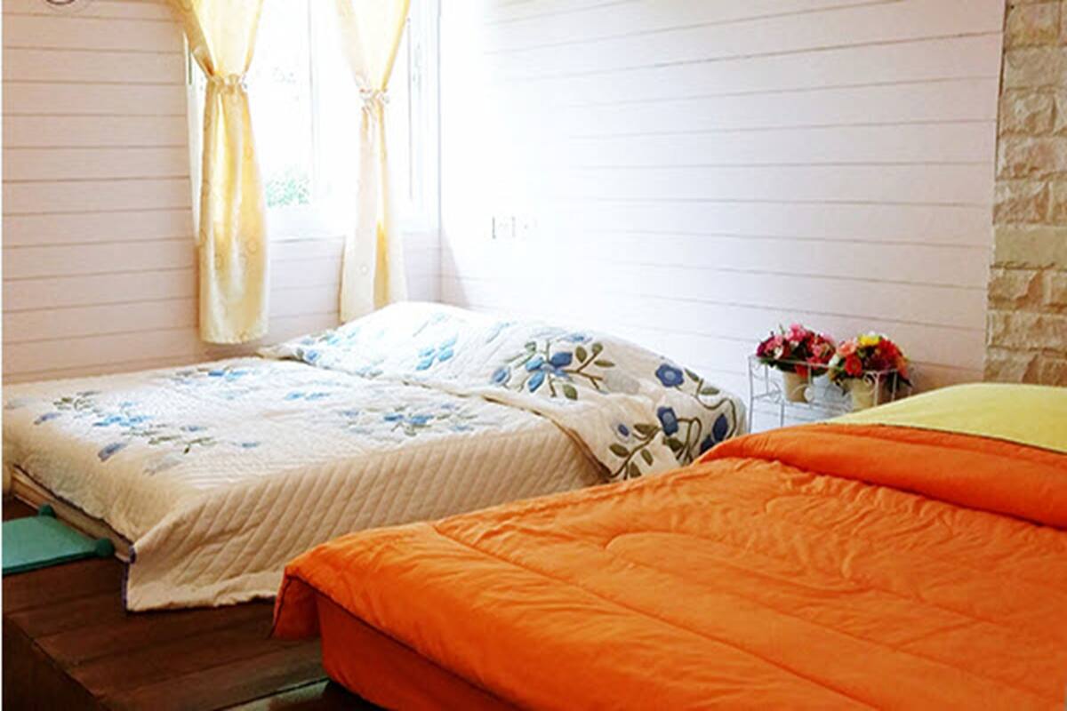 Quarto com duas camas, janela com cortinas e uma mesinha com flores.