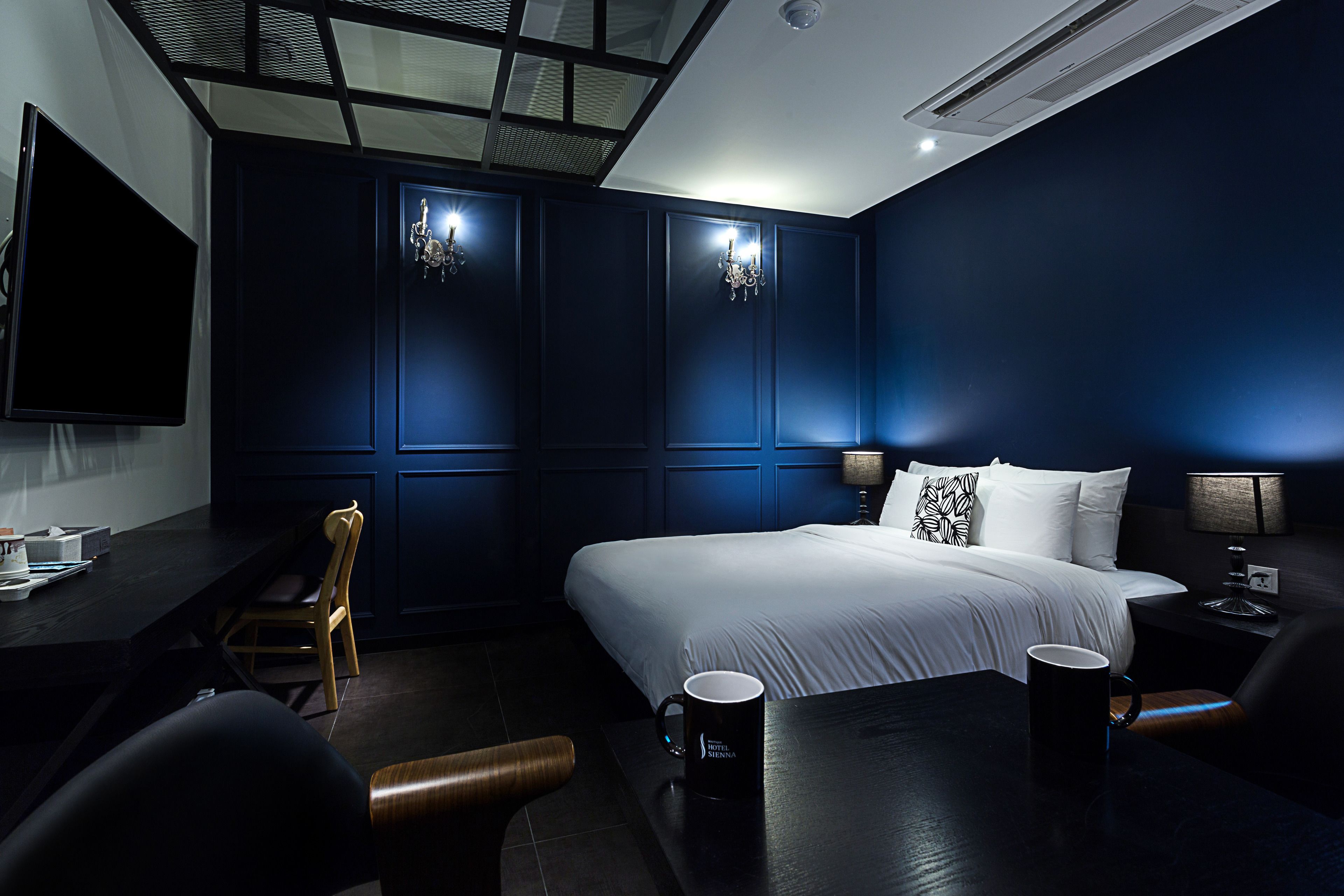 Quarto de hotel moderno com uma cama grande, luminárias de cabeceira, uma mesa e uma cadeira.