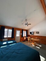 Quarto com duas camas, uma mesa de jantar com cadeiras, um ventilador de teto e uma televisão na parede.