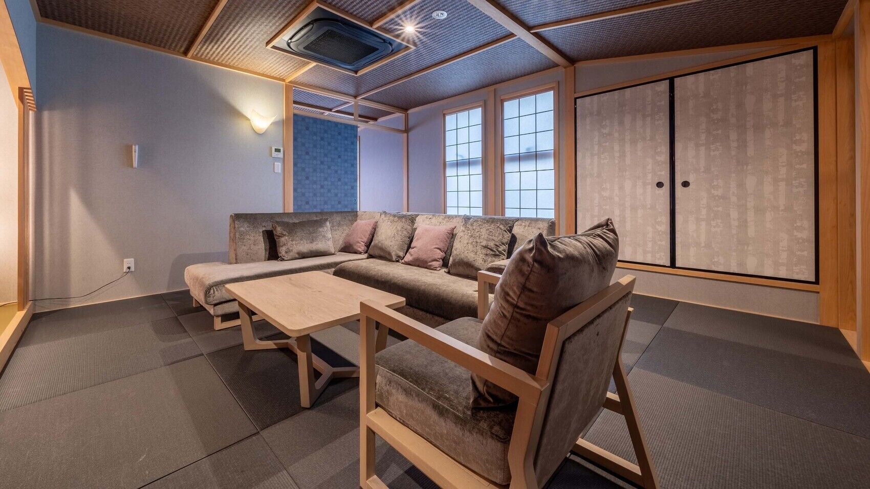 Quarto com sofá, uma cadeira de madeira, uma mesa pequena e uma porta deslizante.