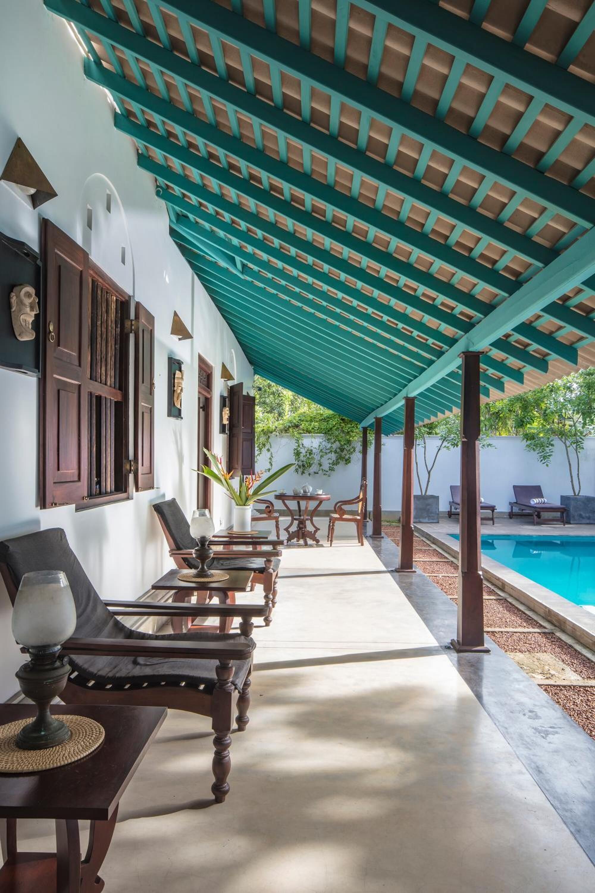 Área de estar coberta ao ar livre, com mobiliário de madeira e piscina ao fundo.