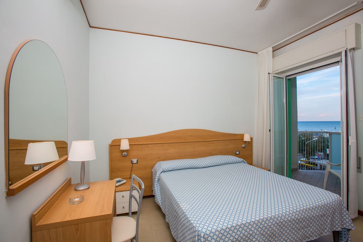 Quarto de hotel com cama, escrivaninha, cadeira, espelho e varanda com vista.