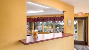 Bancada de recepção com um vaso de vidro cheio de frutas, uma janela com vista para o exterior e um sinal de saída.