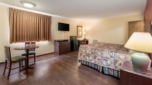 Quarto de hotel com cama, escrivaninha, cadeira, televisão e luminária.