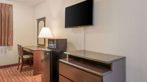 Quarto de hotel com escrivaninha, cadeira, micro-ondas, TV de tela plana, luminária e espelho.