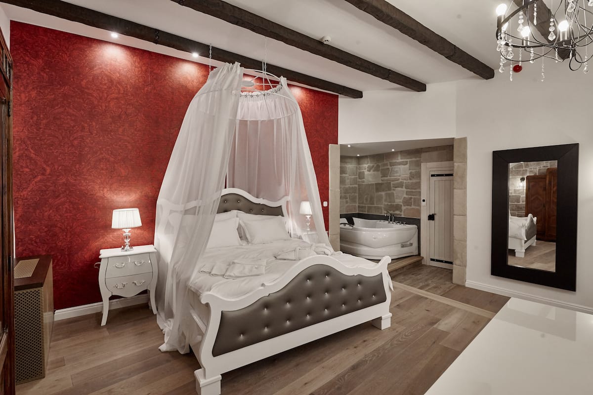 Quarto com cama de dossel, parede de pedra, banheira e espelho.