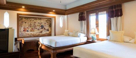 Quarto de hotel com duas camas, piso de madeira, um quadro tradicional grande e um ventilador de teto.
