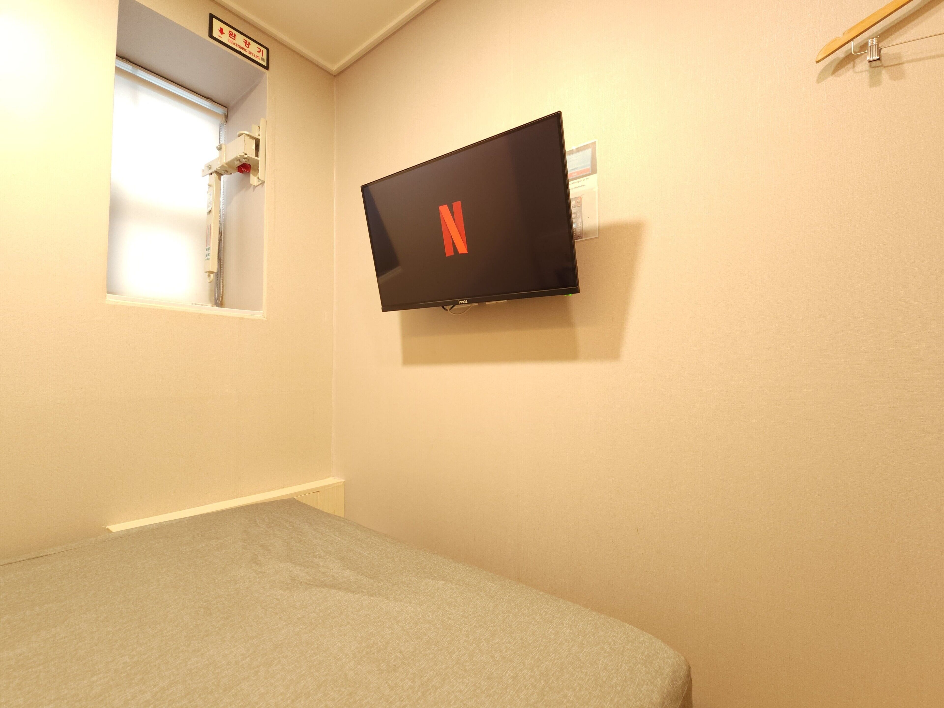 Quarto com cama, televisão na parede e janela com persianas.