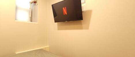 Quarto com cama, televisão na parede e janela com persianas.