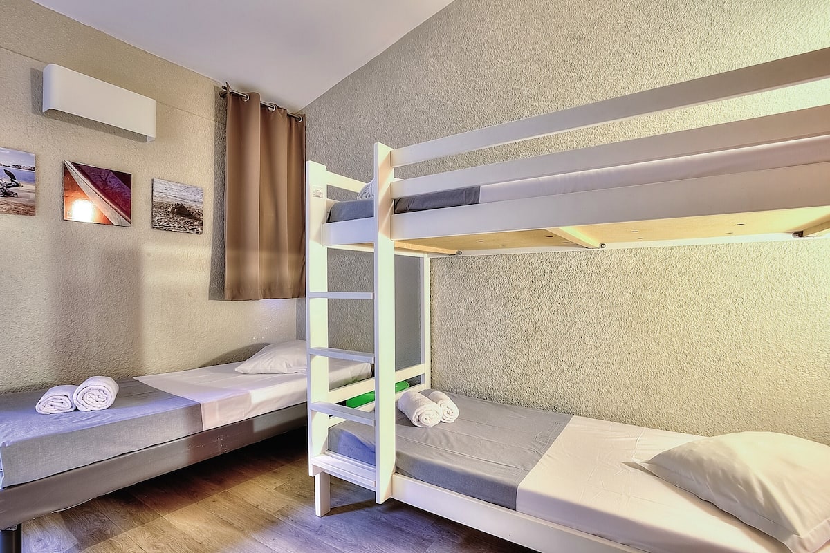 Quarto com beliche, uma escada, duas camas e ar condicionado fixado na parede.