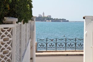 Vista costeira com um edifício branco, uma cerca de metal e um corpo de água.