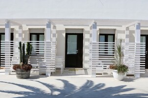 Um edifício moderno com paredes externas brancas, portas pretas e estruturas de treliça brancas. Há plantas em vasos com cactos e outras folhagens em frente às portas.