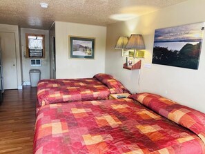 Quarto com cama, mesinha, luminária, quadro na parede e janela.