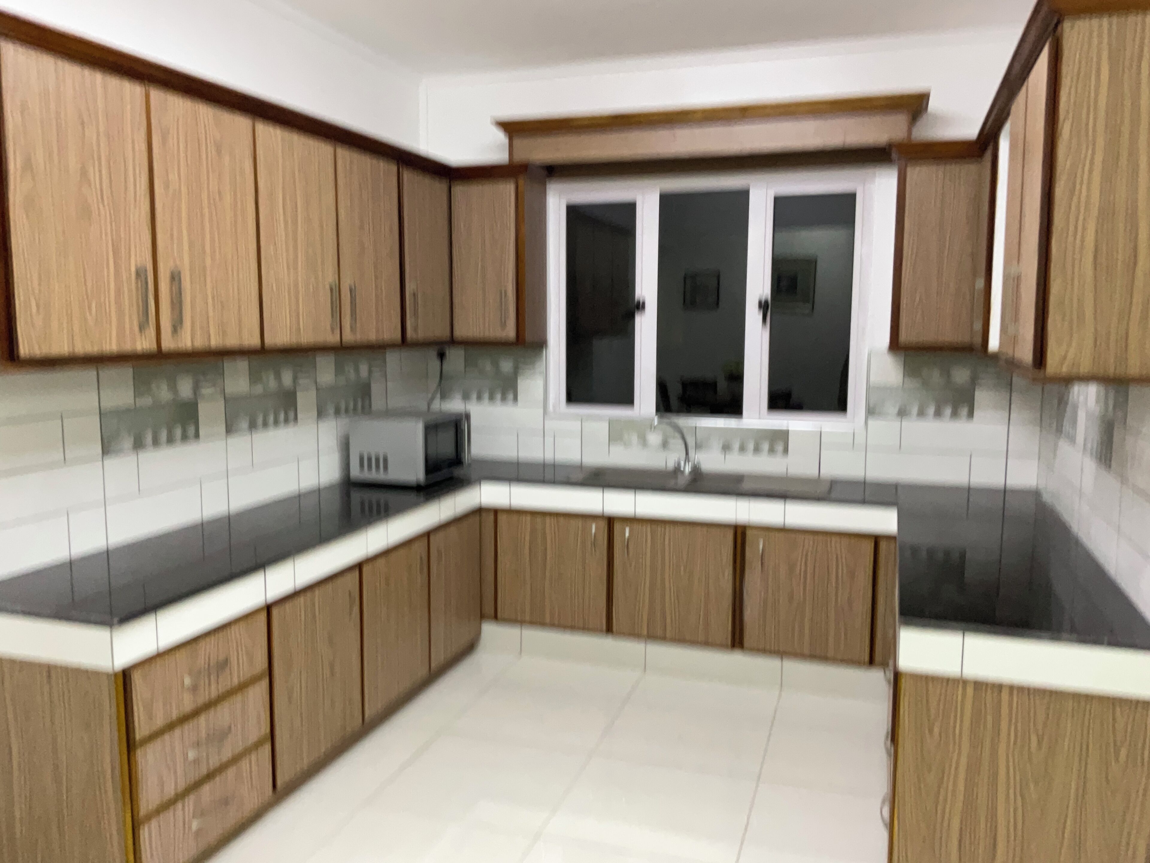 Cozinha com armários de madeira, bancada preta e micro-ondas.