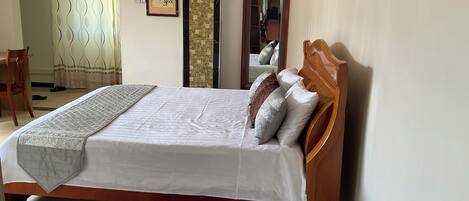 Uma cama bem arrumada com cabeceira de madeira, uma mesa de cabeceira e um espelho na parede.