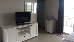 Quarto de hotel com televisão em um armário branco, uma pequena geladeira e uma janela com cortinas.