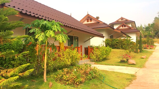 Fileira de casas com estilo arquitetônico uniforme, com telhados inclinados e jardim bem cuidado, com diversas plantas e um caminho.