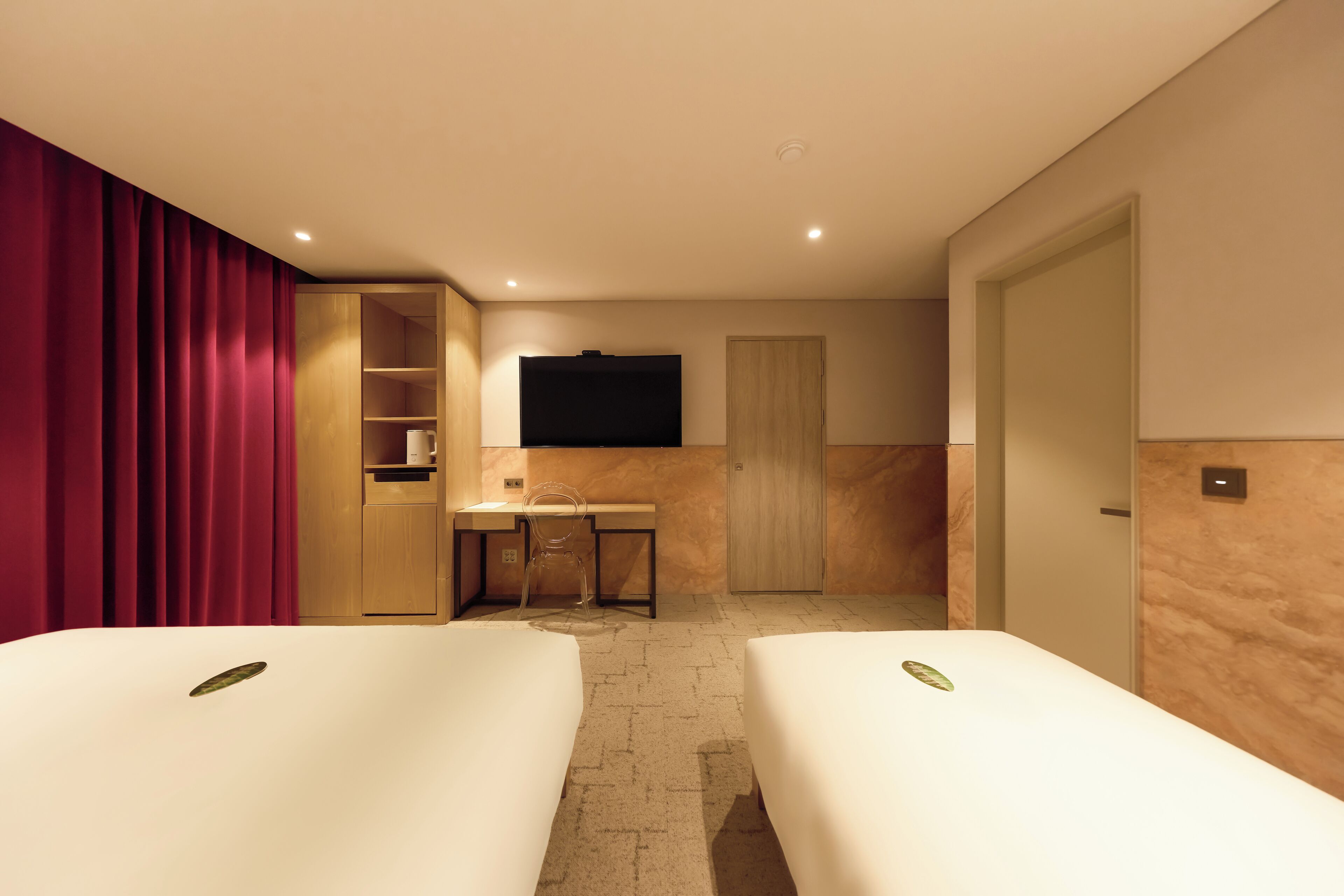 Quarto de hotel com duas camas, uma escrivaninha, televisão e zona de chuveiro.