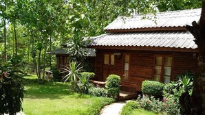 Uma cabana de madeira com telhado de metal corrugado, rodeada por vegetação exuberante e um gramado bem cuidado.