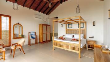 Um quarto espaçoso com uma cama de madeira com dossel, uma cadeira de madeira, uma mesinha e um ventilador de teto.