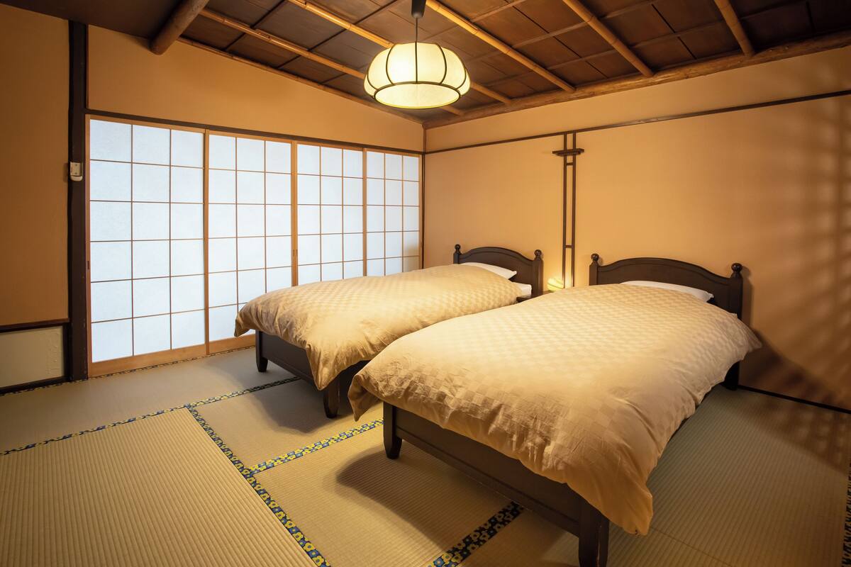 Um quarto japonês tradicional com tatame, duas camas de madeira, um biombos shoji e um lustre suspenso.