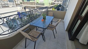 Varanda com mesa de vidro e cadeiras de vime, delimitada por uma grade de metal.