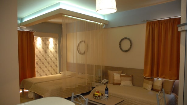 Quarto de hotel com duas camas, uma mesa pequena e uma cadeira. Há uma lâmpada sobre a mesa e uma garrafa de água.