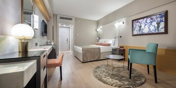 Quarto de hotel moderno com cama, escrivaninha, cadeira e uma pequena mesa. Há um quadro na parede e um tapete no chão.