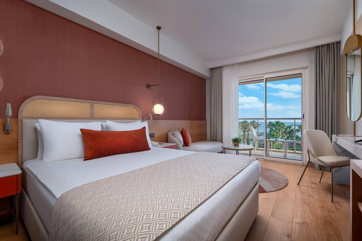 Quarto de hotel com uma cama grande, televisão, escrivaninha e varanda com vista.