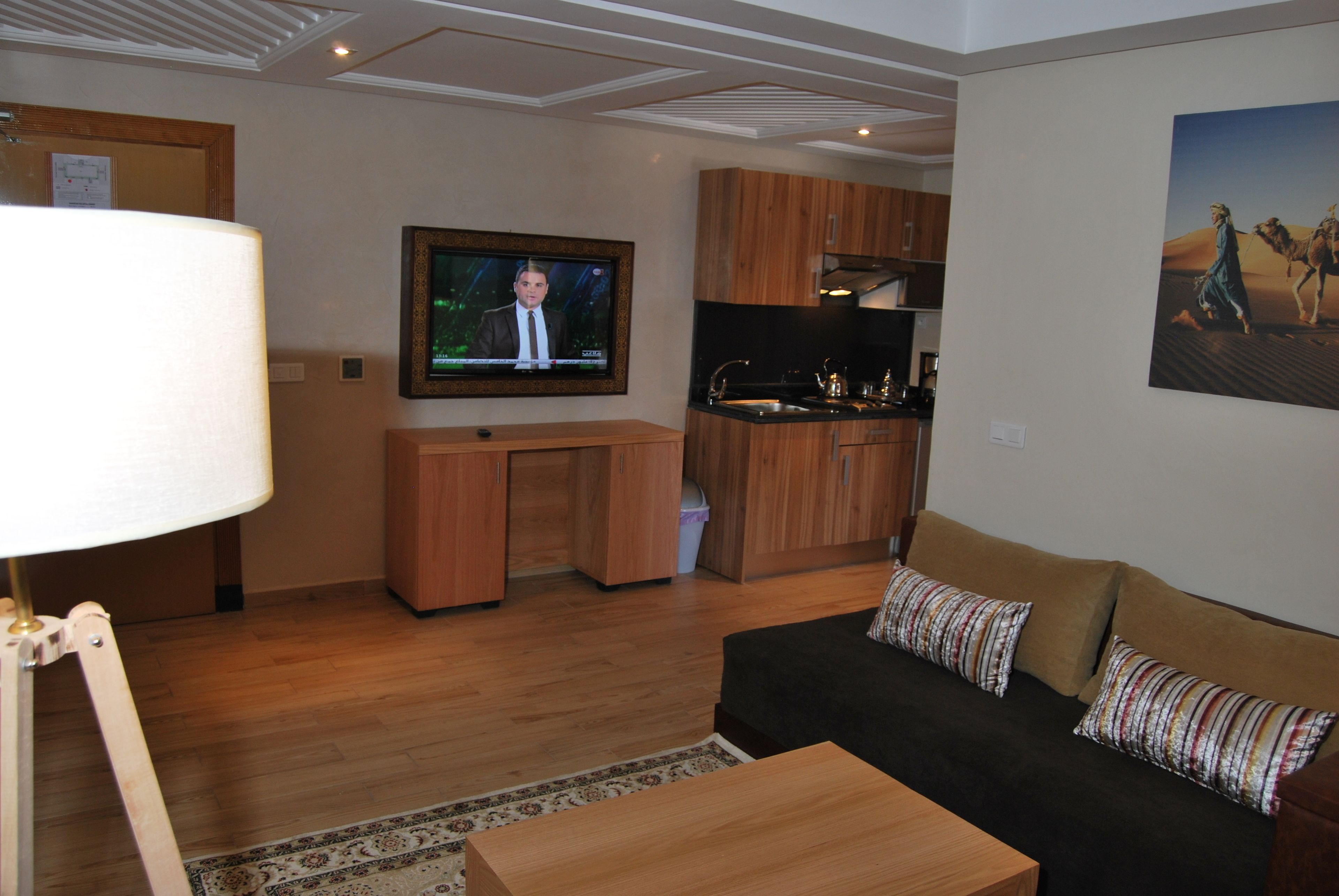 Uma sala de estar moderna com sofá, mesa de centro e televisão. Há uma área de cozinha com armários de madeira e pia.