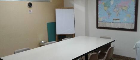 Uma sala de conferências com uma mesa comprida, cadeiras, um quadro branco, uma tela de projetor com um mapa-múndi e um aviso de proibido fumar.