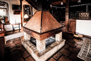Um forno de tijolos tradicional com telhado inclinado, localizado em um ambiente com piso de madeira e tapete estampado.