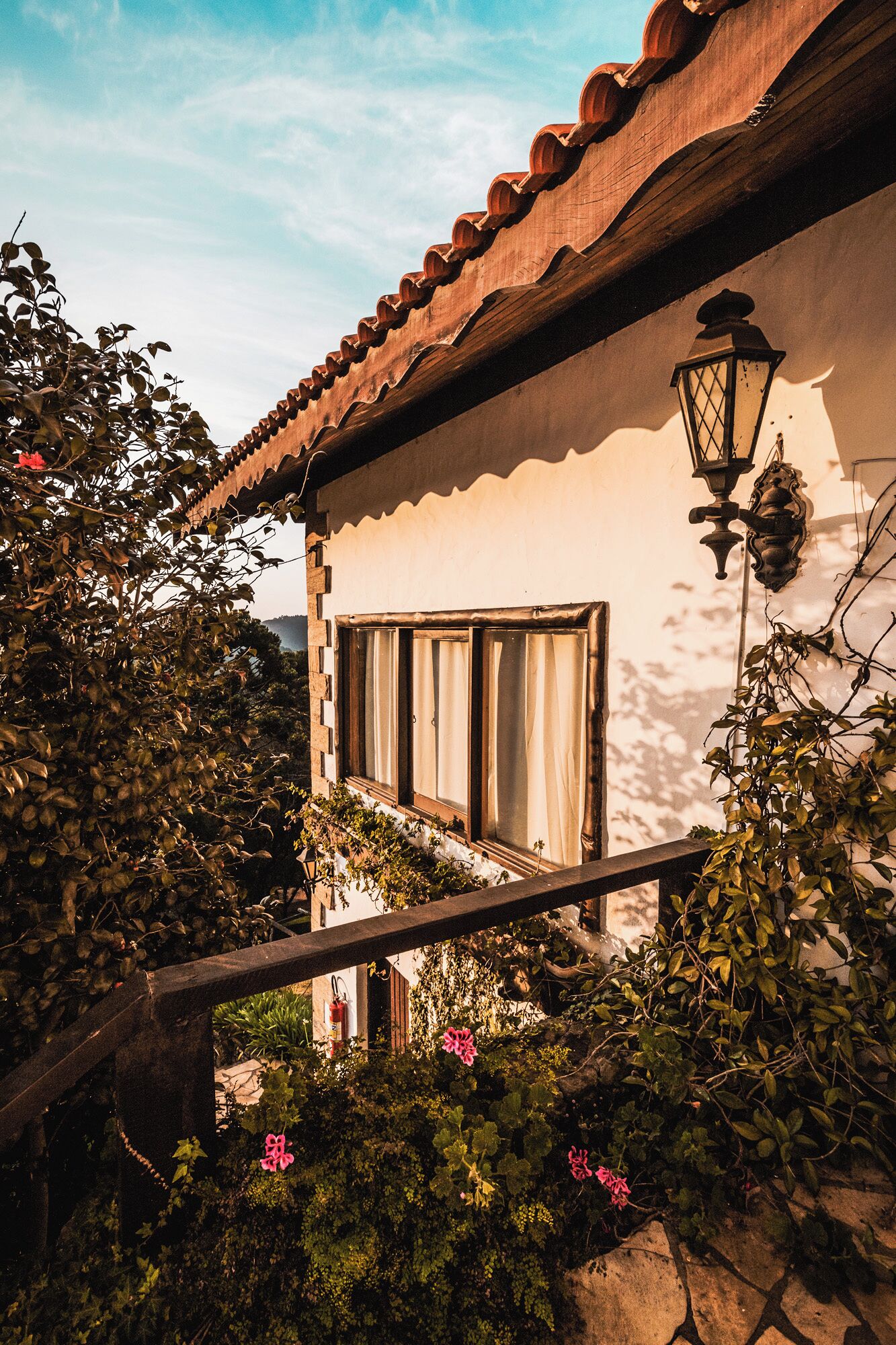 Um edifício com telhado de azulejos, uma janela com cortinas e um candeeiro.