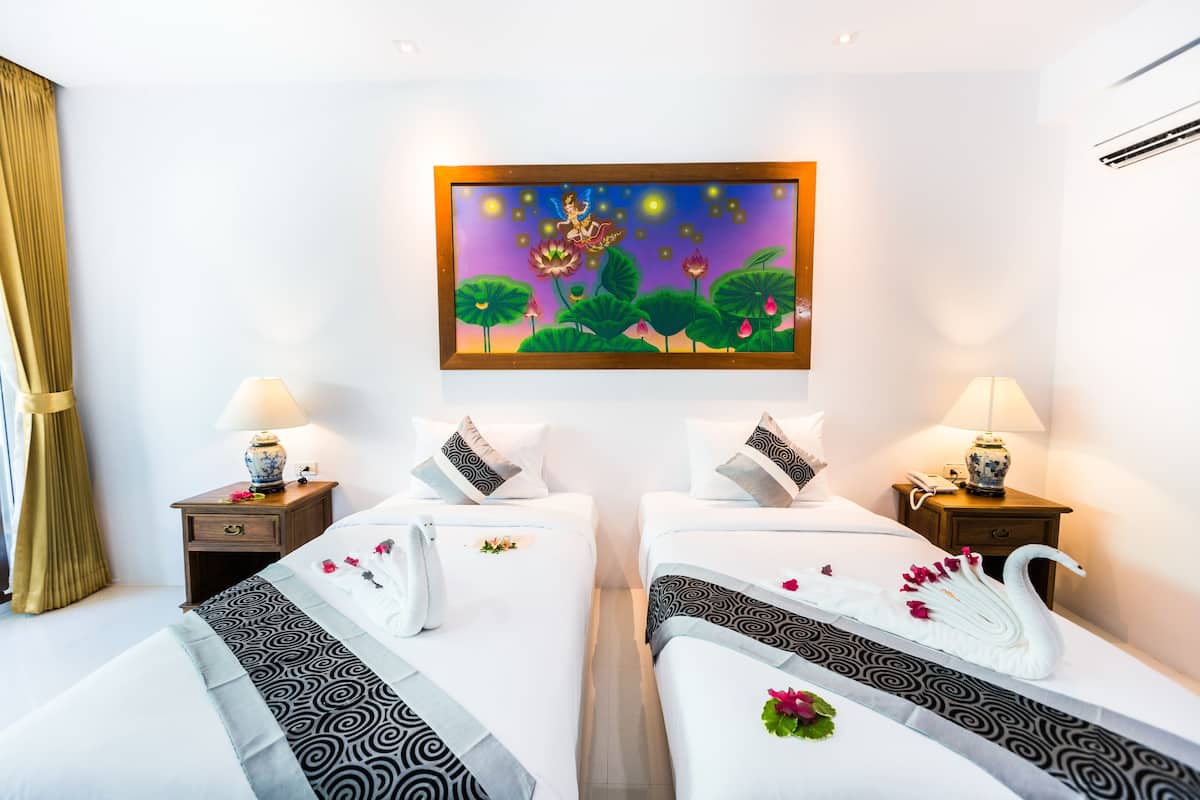 Quarto de hotel com duas camas, uma mesa de cabeceira com abajur, um quadro na parede e toalha em forma de cisne sobre as camas.