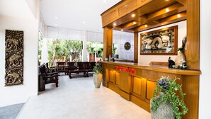 Uma área de recepção com balcão de madeira, mesa de atendimento e um vaso grande com plantas.