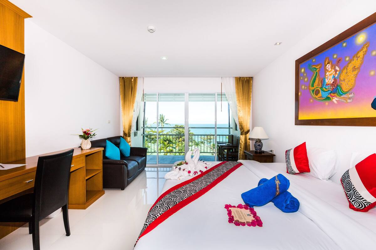 Quarto de hotel com cama, escrivaninha, cadeira, sofá, televisão e um quadro.
