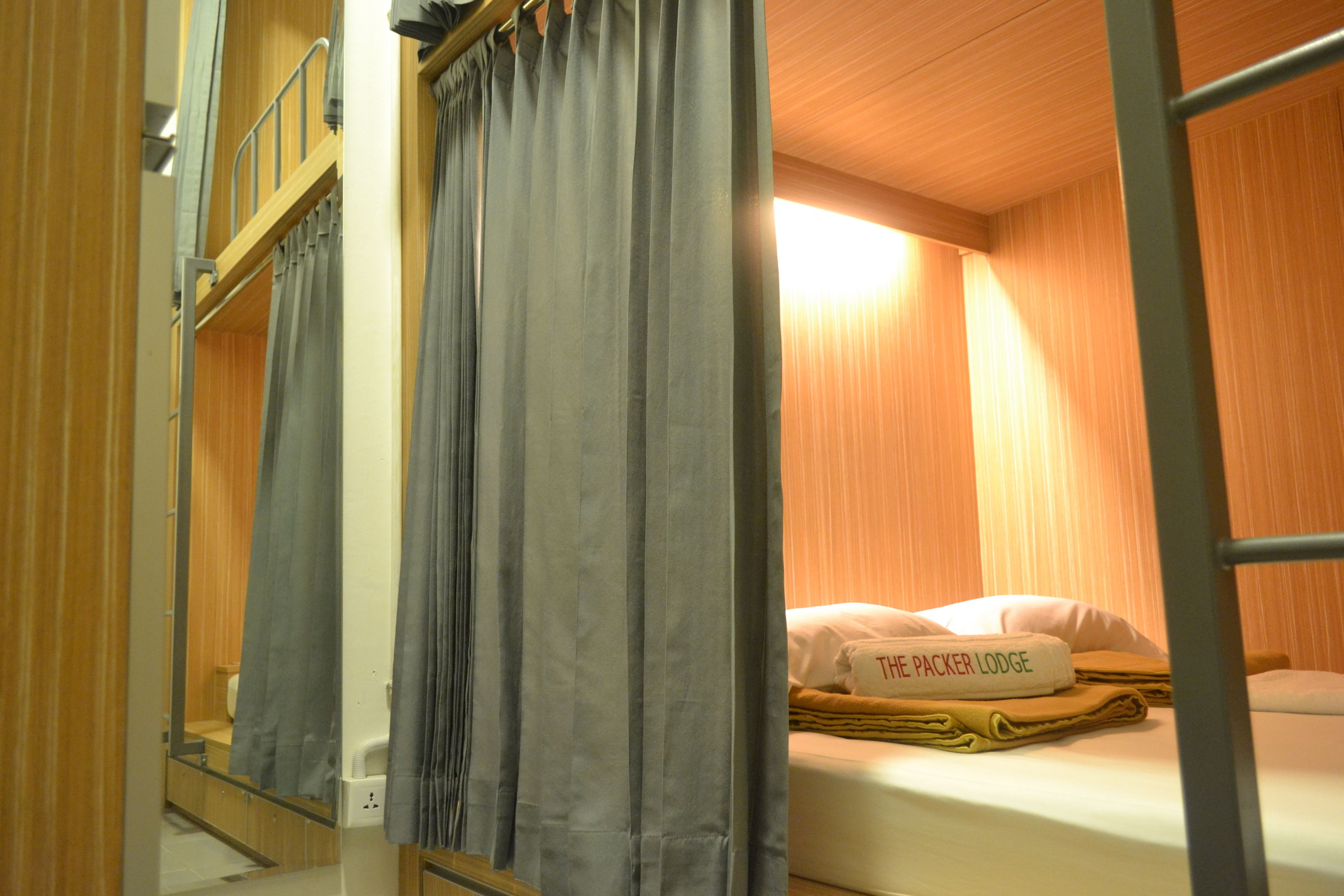 Uma cama beliche com cabeceira, um banheiro com cortina de chuveiro e uma cama com travesseiro rotulado como "THE PACKER LODGE".