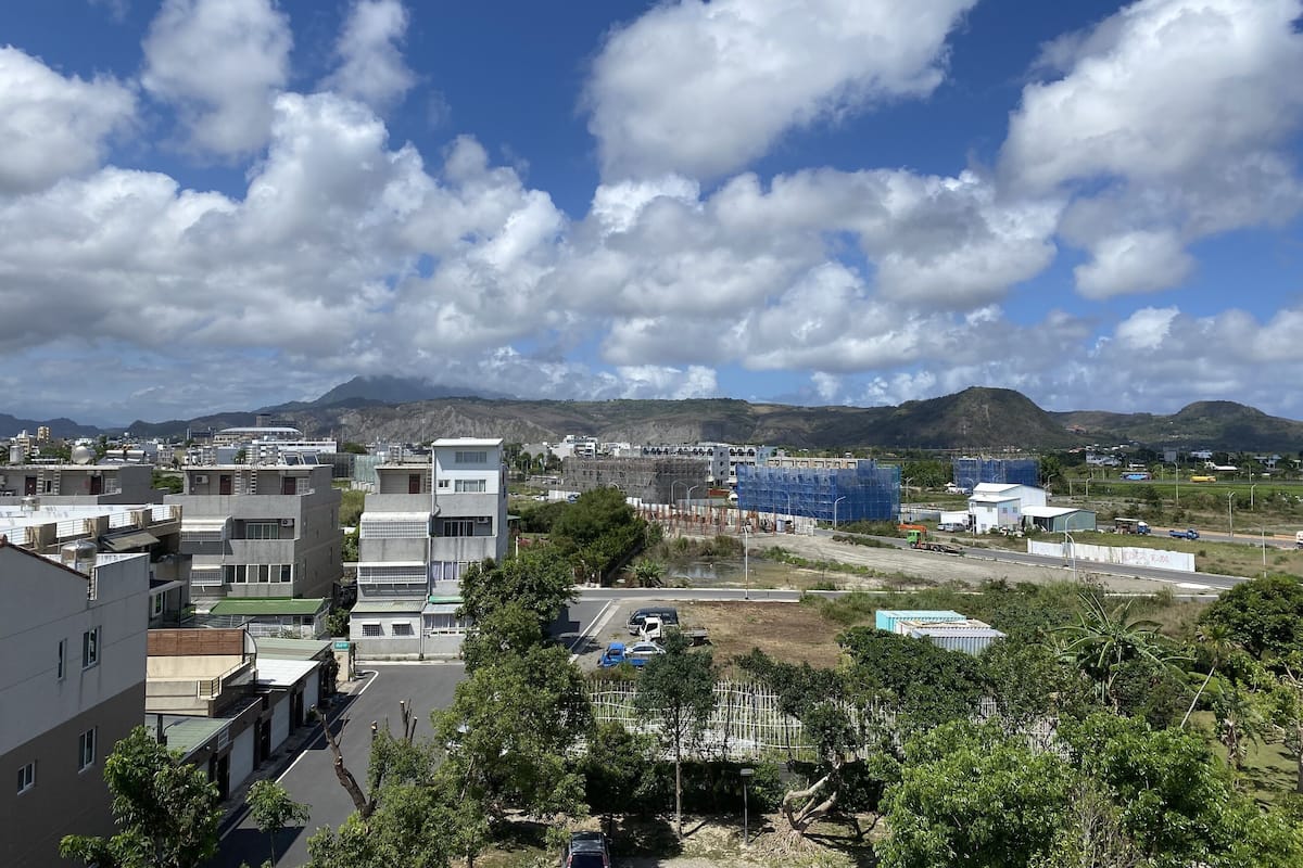 Paisagem urbana com edifícios modernos, céu claro e montanhas ao fundo.