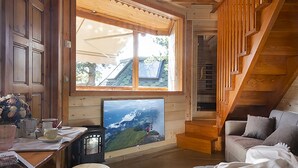 Interior acolhedor de uma cabana com uma escada de madeira, televisão na parede e uma área de refeições com mesa e cadeiras.
