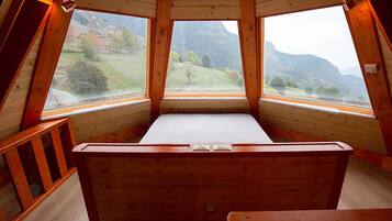 Uma cabana de madeira com cama e janelas amplas que oferecem vista para uma paisagem montanhosa.