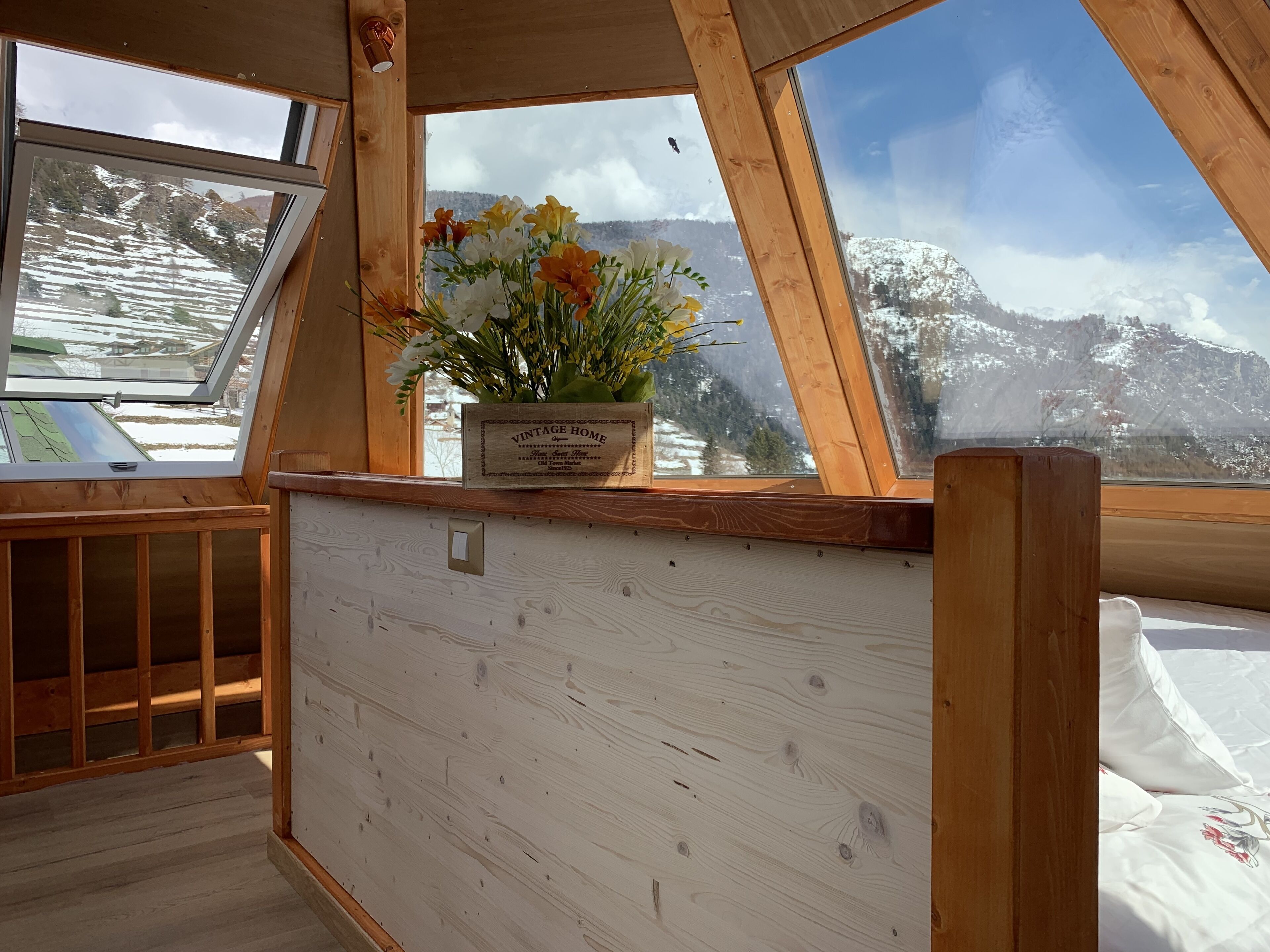 Interior em madeira com claraboia, um banco de madeira e janela com vista para montanhas cobertas de neve.