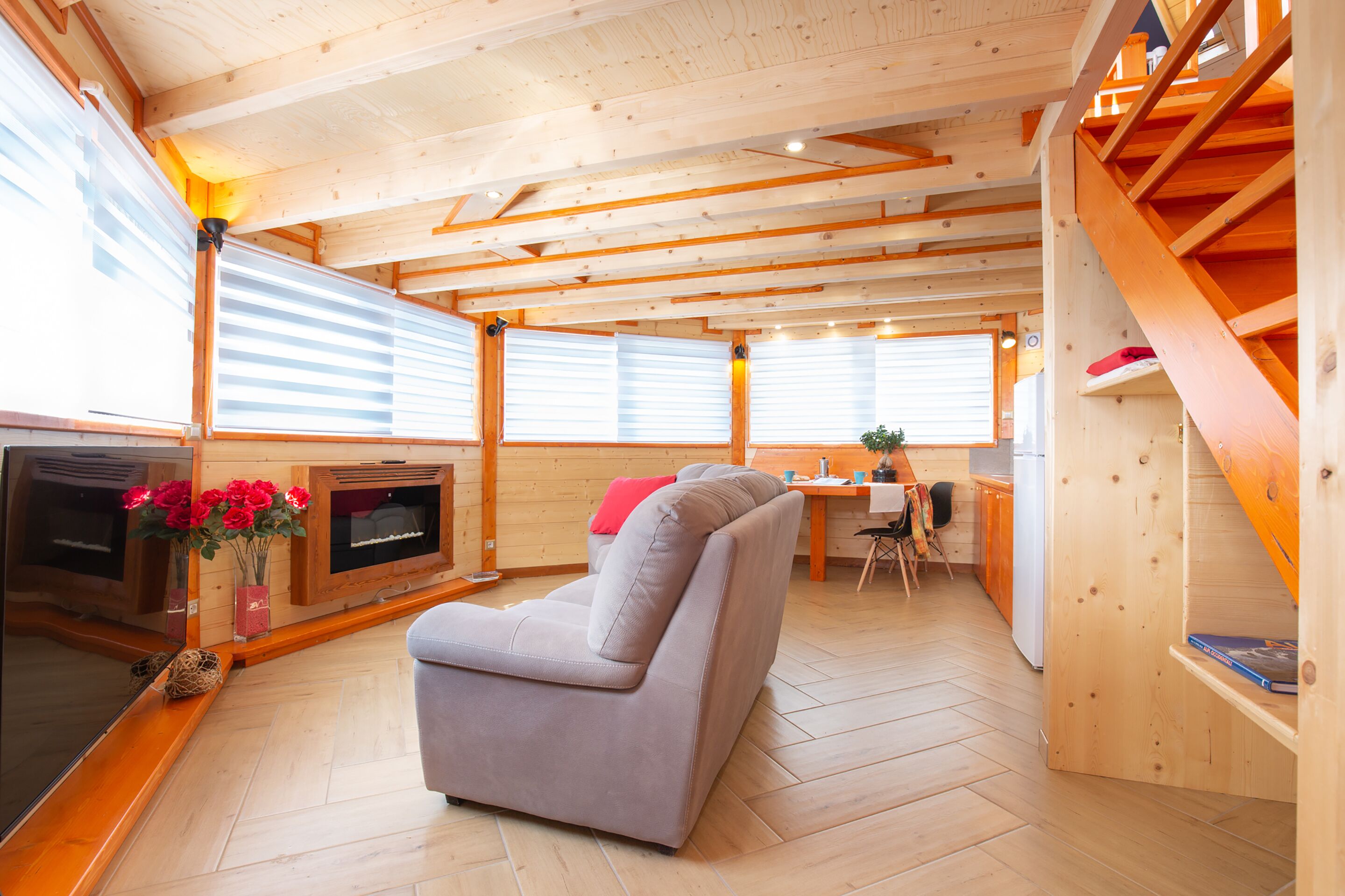 Interior acolhedor de uma cabana com sofá, piso de madeira, lareira e área de jantar.