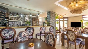 Um restaurante com área de bar, cadeiras de madeira com estofamento floral e uma grande tela de televisão.