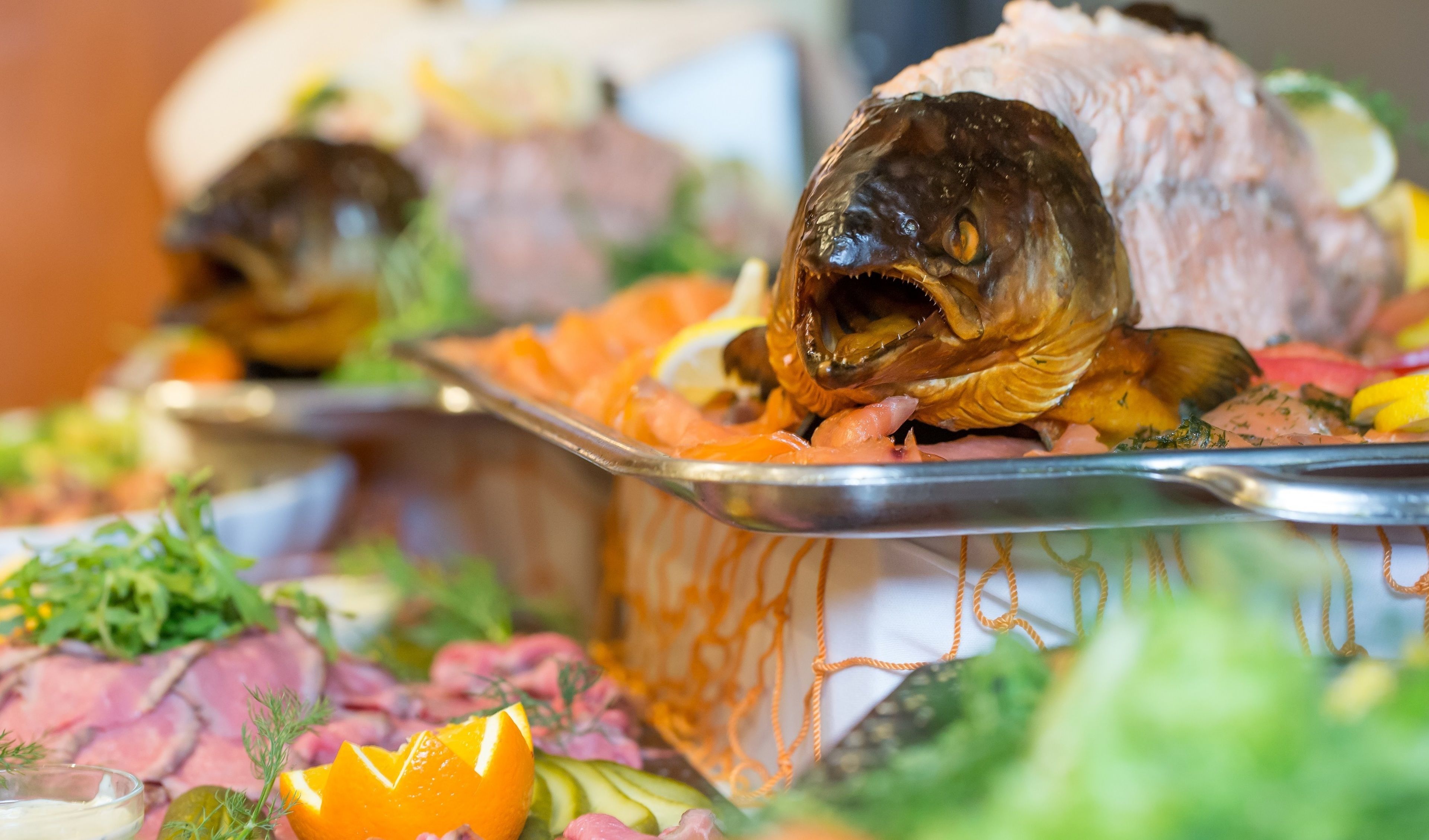 Buffet com diversos pratos, incluindo peixe, legumes e um assado grande.