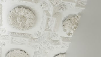 Teto com intrincados padrões decorativos brancos, incluindo motivos florais e formas geométricas.