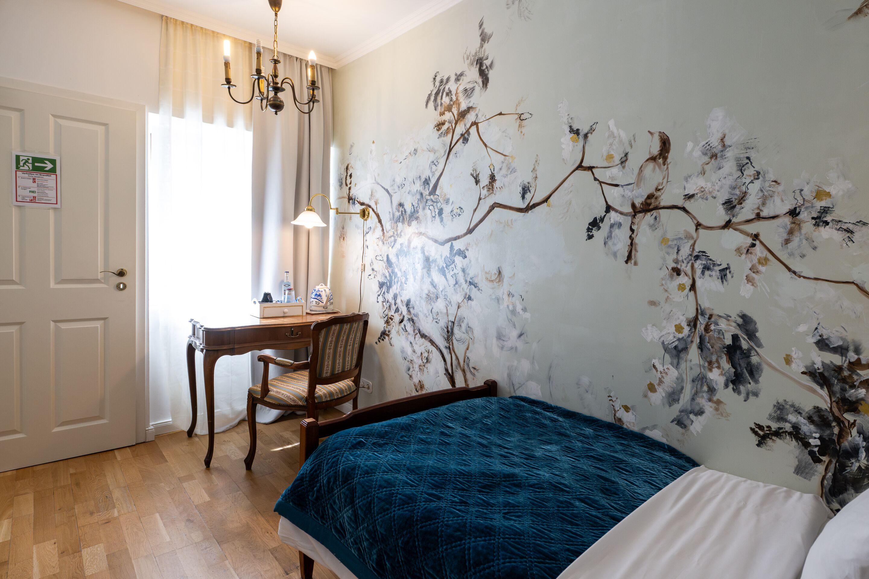 Quarto com cama, escrivaninha, cadeira e parede com um mural floral.