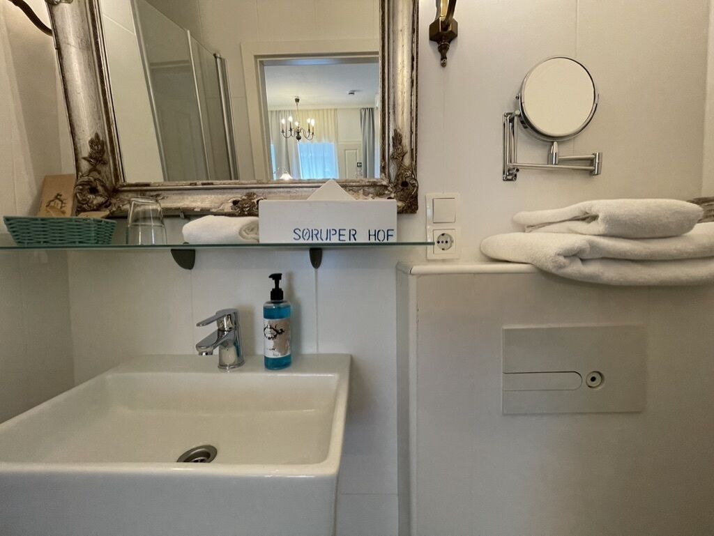 Uma casa de banho com um espelho grande, uma pia com torneira, um dispensador de sabonete e um porta-toalhas.