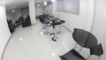 Uma área de jantar moderna com mesa redonda e cadeiras, um bar com bancos e uma sala de estar com sofás e televisão.
